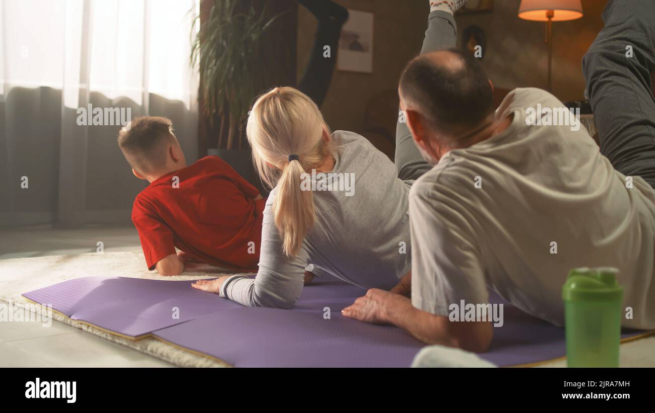 Grandparents and grandson excercising at home and doing a leg muscle ...