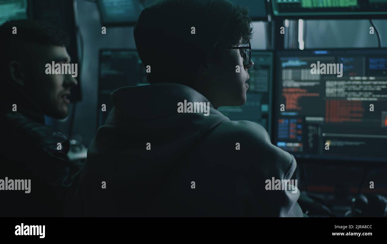 Young male hacker in glasses looking at screen and talking with ...