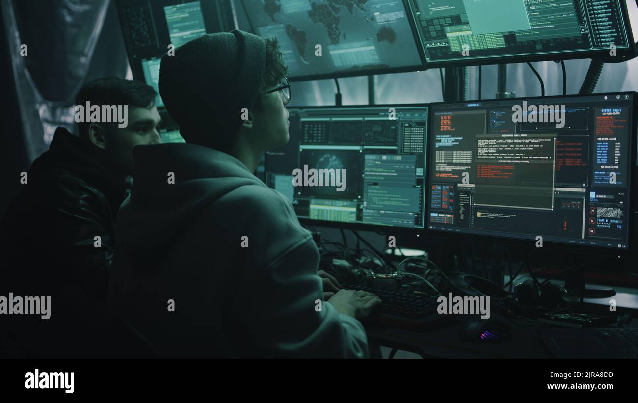 Two hackers in casual clothes cracking classified files on computer and ...