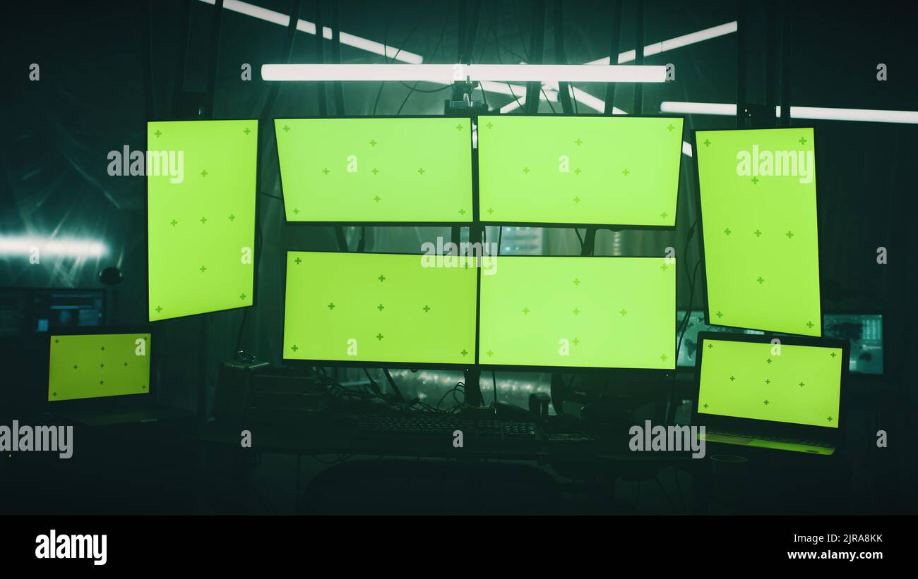 Modern computers with green screens placed on desk in dark room with ...