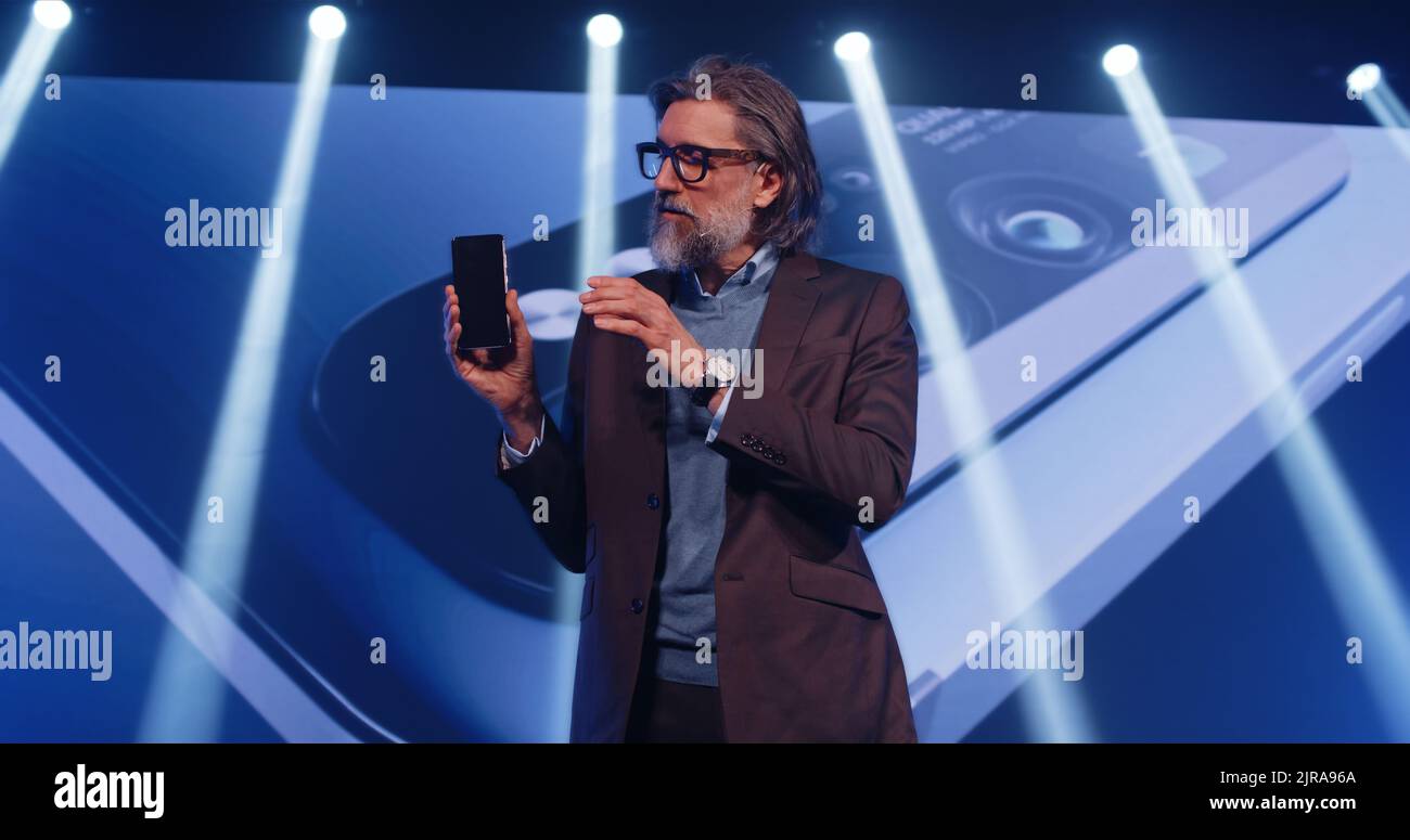 Presenter standing on stage with a new contemporary smartphone at the ...
