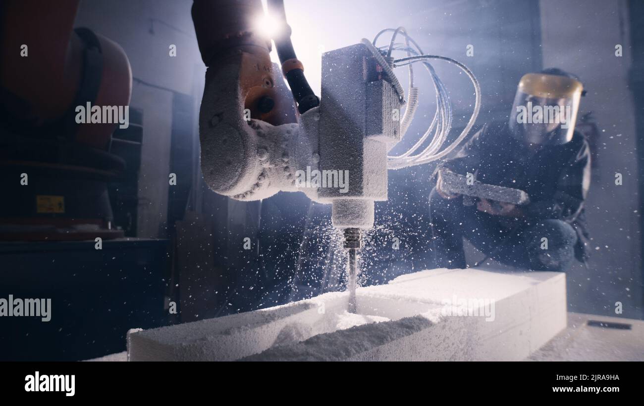 Zoom out view of man in face shield and respirator watching robotic arm ...