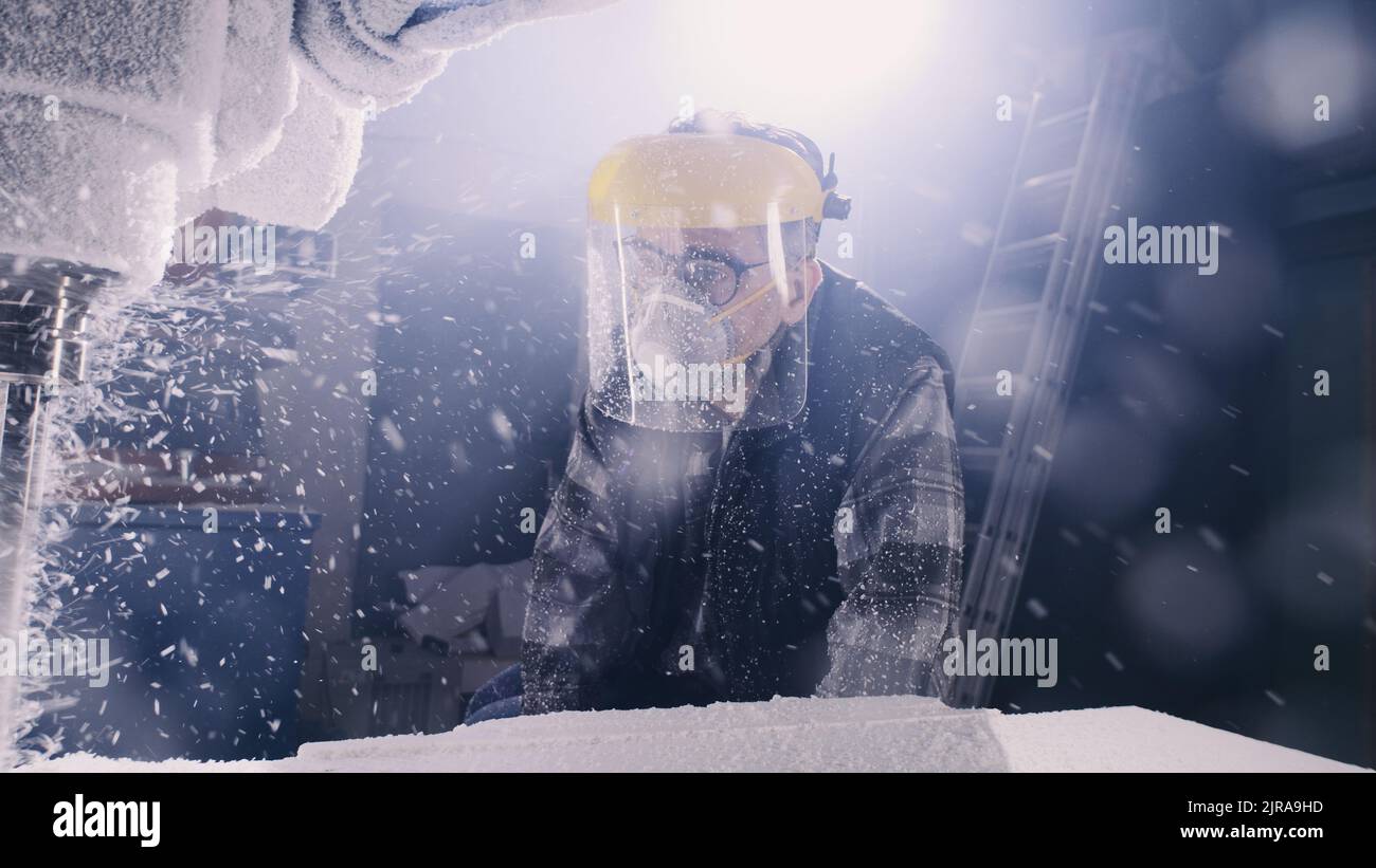 Zoom out view of man in face shield and respirator watching robotic arm ...