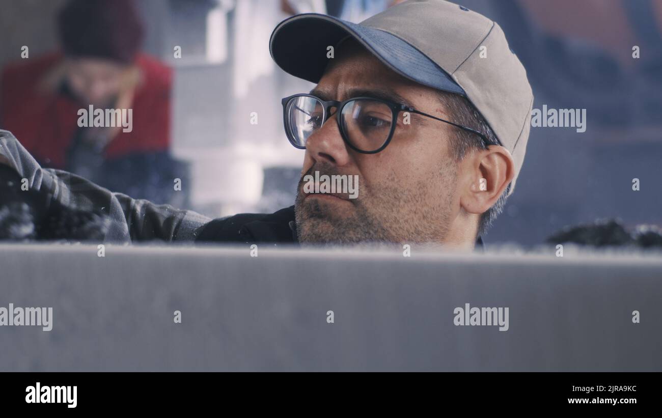 Rack focus of mature man in glasses and cap blowing off sweeping dust ...