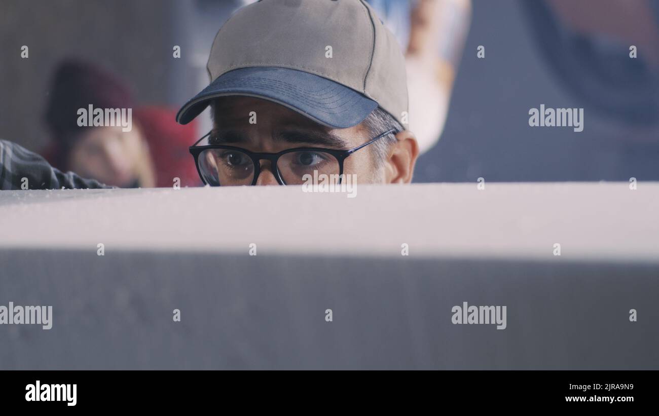 Middle aged male worker in glasses and cap inspecting plastic block ...