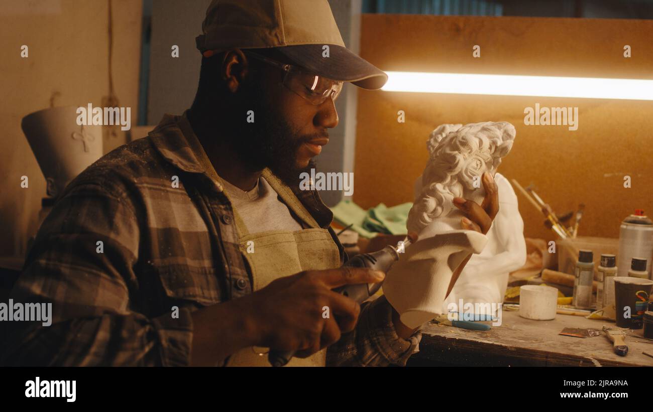 African American craftsman in checkered shirt and cap polishing half of ...