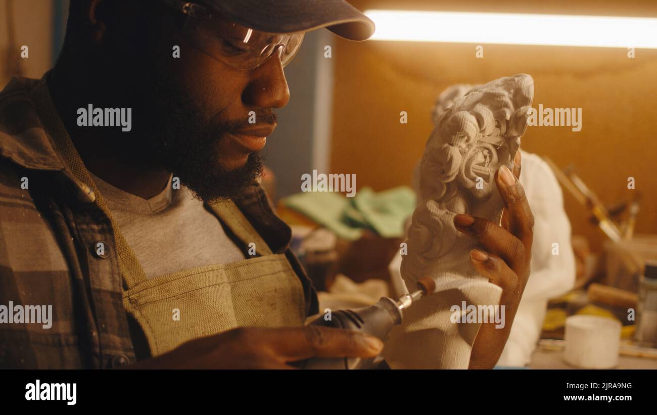 African American craftsman in checkered shirt and cap polishing half of ...