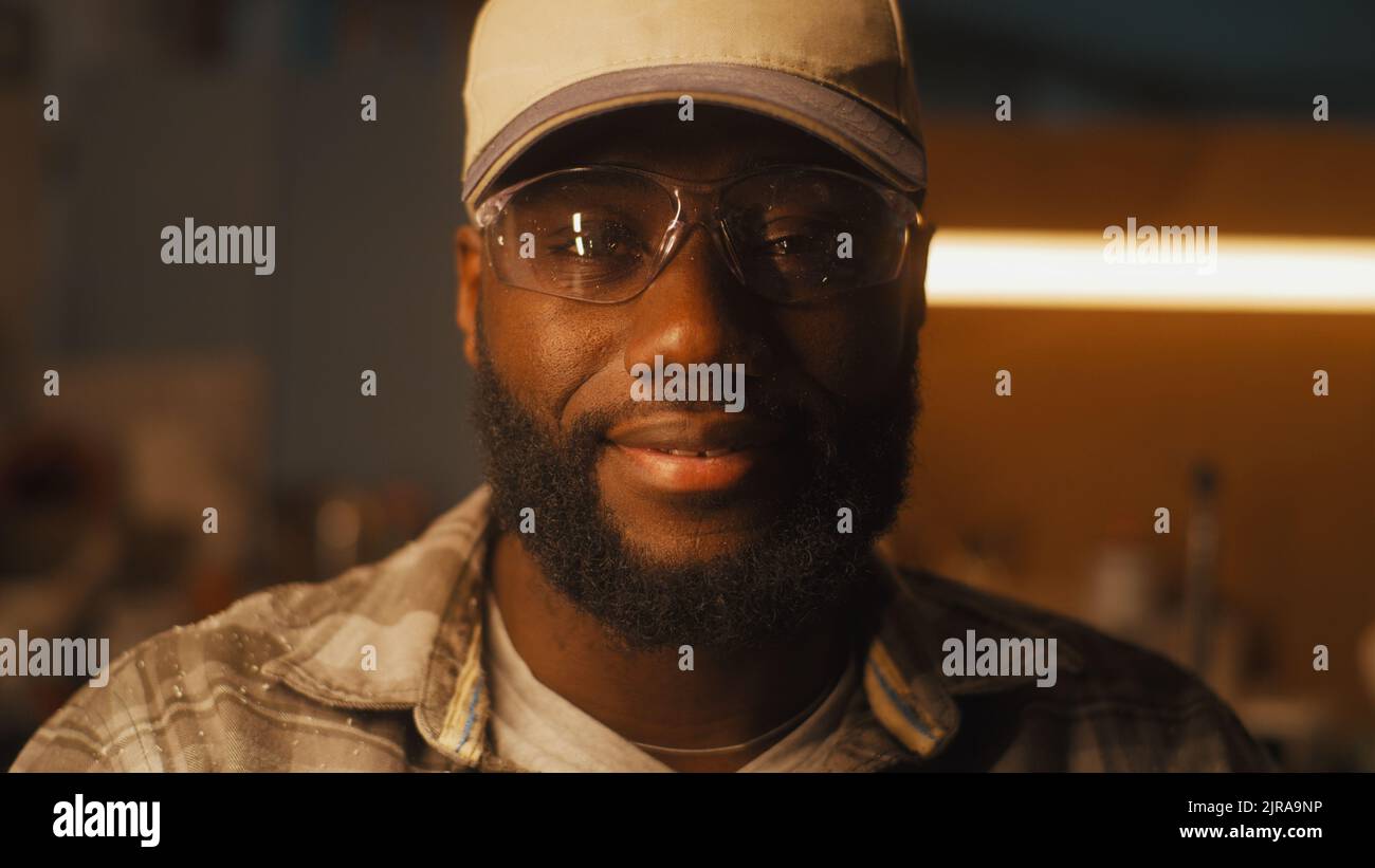 Positive African American craftsman in cap and goggles smiling and ...