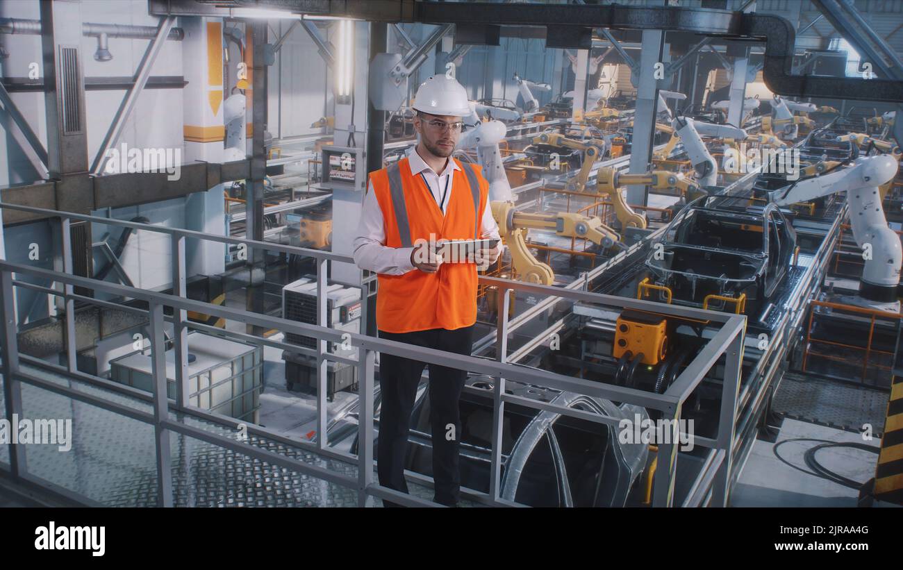 Male employee in uniform and hardhat browsing tablet against automatic ...