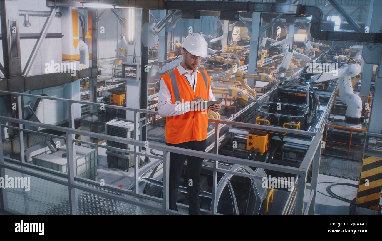 Male employee in uniform and hardhat browsing tablet against automatic ...