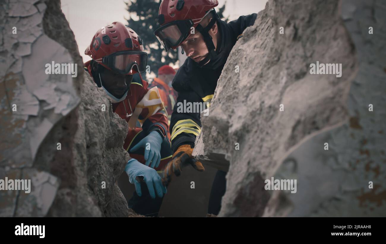 Black rescuer talking with colleague while sitting near rubble and ...