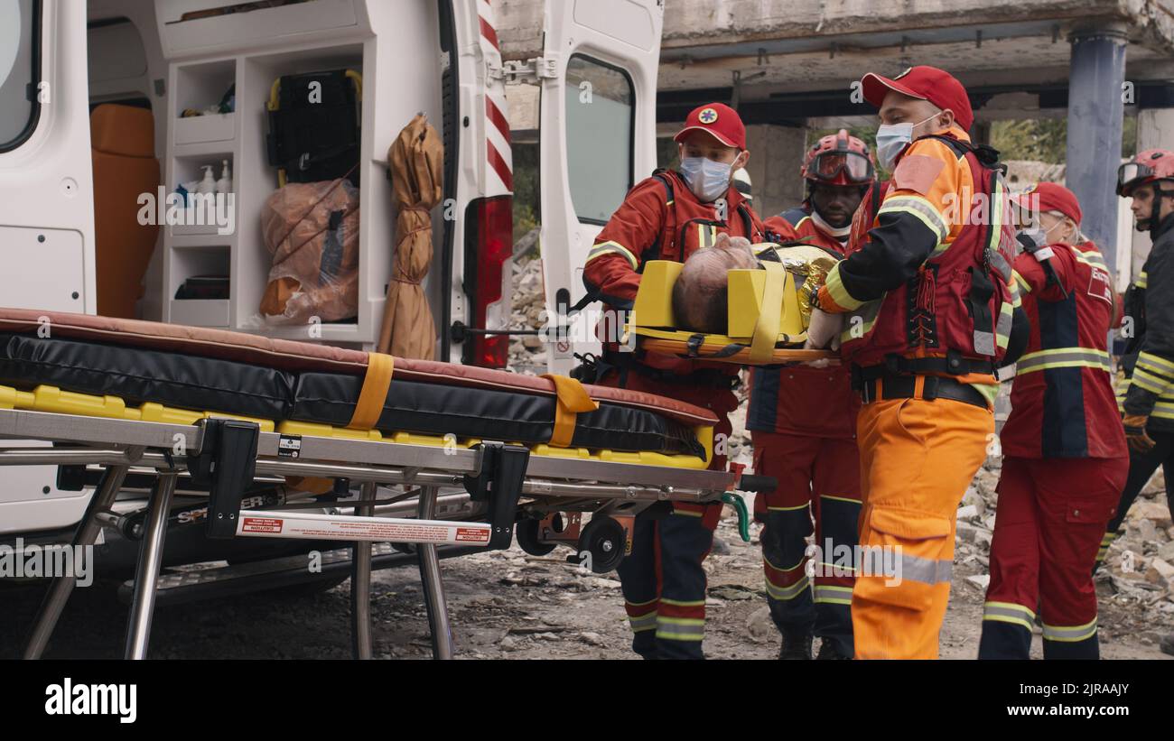 Multiracial team of paramedics in uniform and masks carrying spinal ...