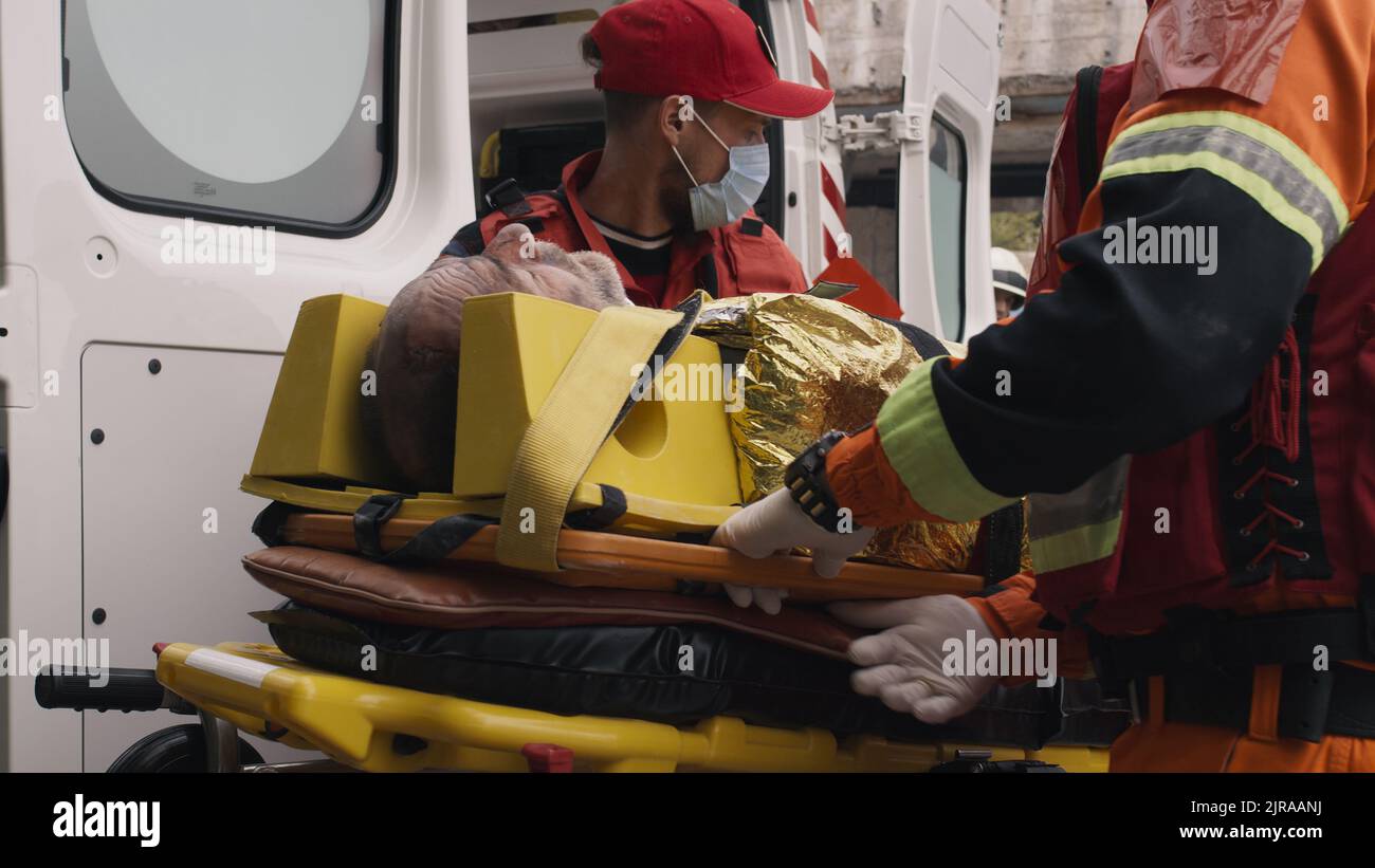 Paramedics putting body of injured survivor into trunk of emergency van ...