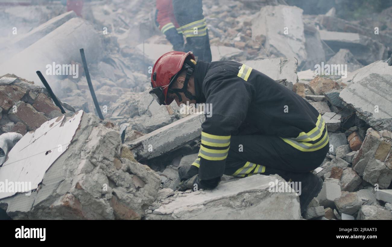 Pan left view of male emergency workers removing concrete rubble in ...