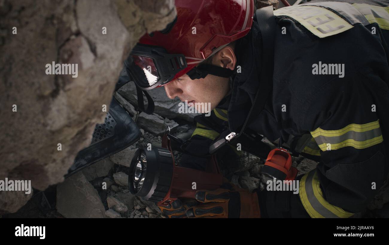 Male rescuer in protective uniform looking at hole under rubble and ...