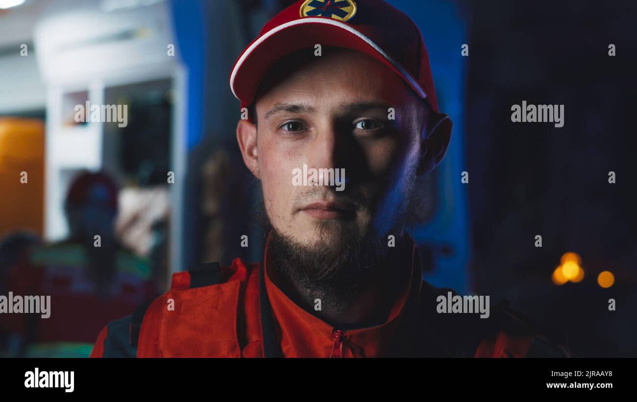 Bearded man in paramedic uniform looking at camera during work on dark ...