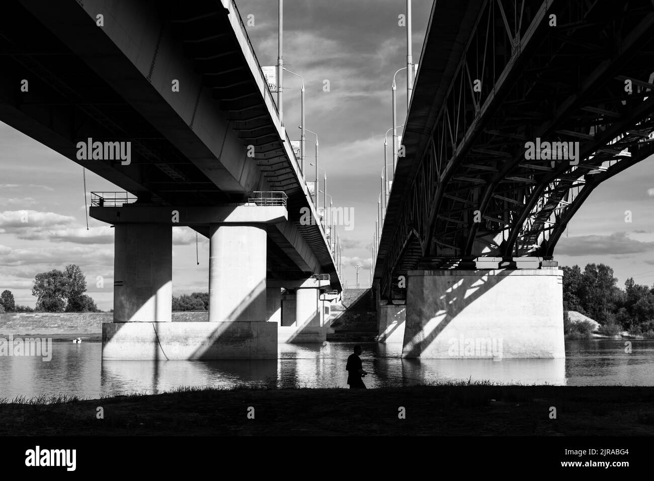 The grayscale of a man's silhouette while fishing by the river under the two bridges Stock Photo ...