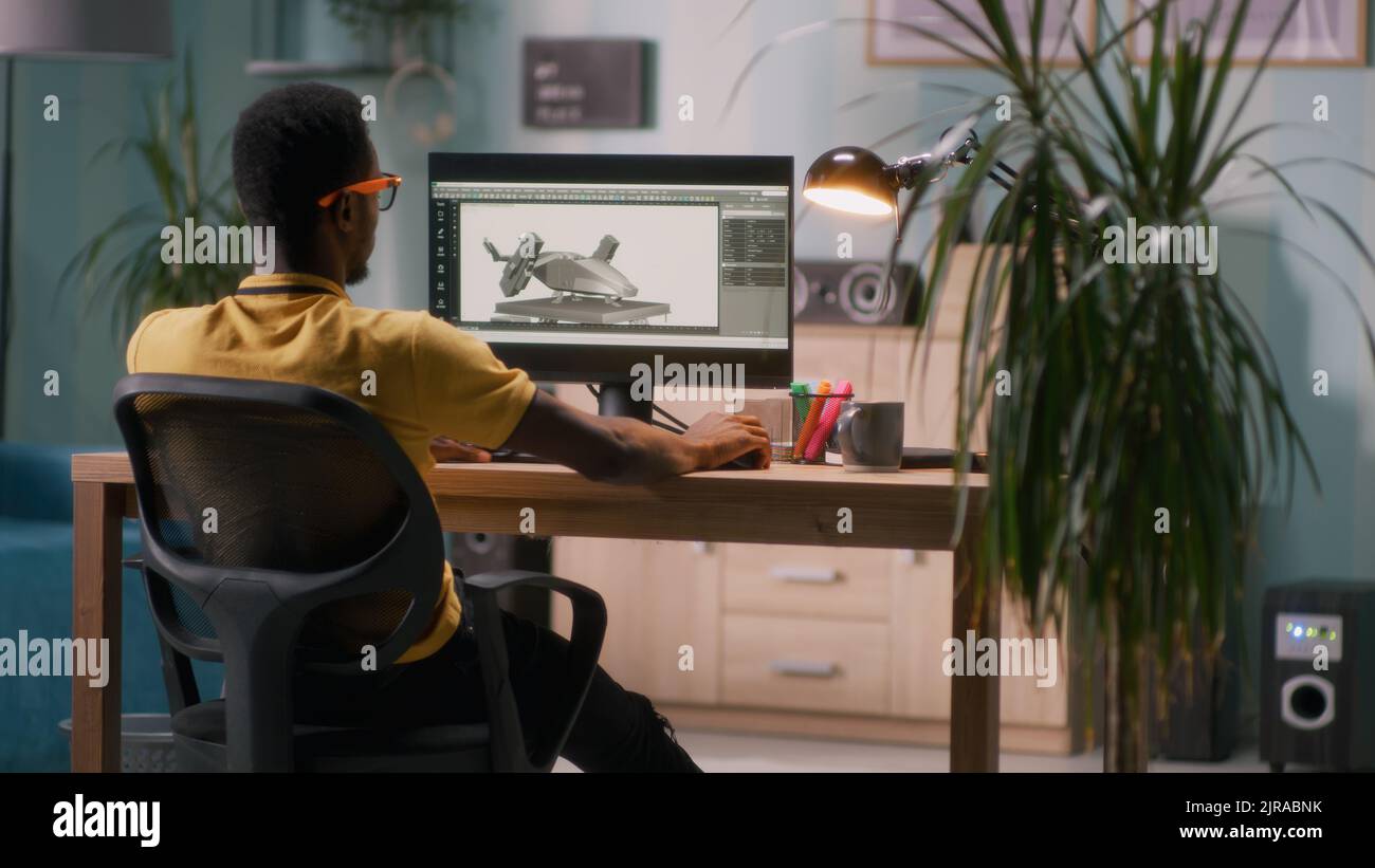 African American man creating 3D model and video for videogame on computer while sitting at ...