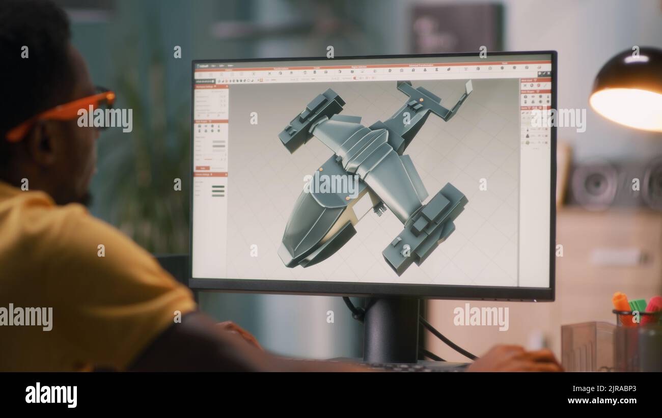 Black man using computer and creating 3D model of futuristic aircraft for videogame or movie ...