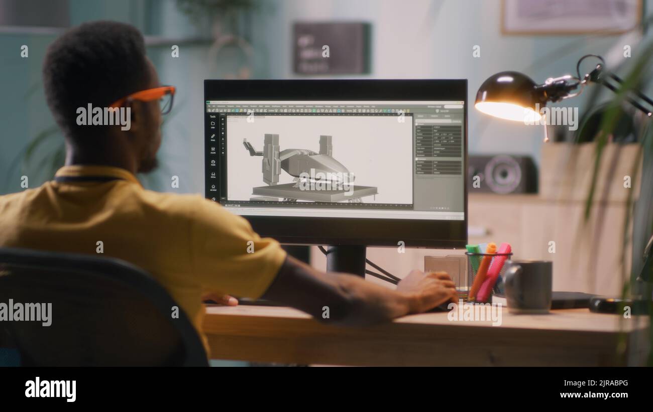 African American man creating 3D model and video for videogame on computer while sitting at ...
