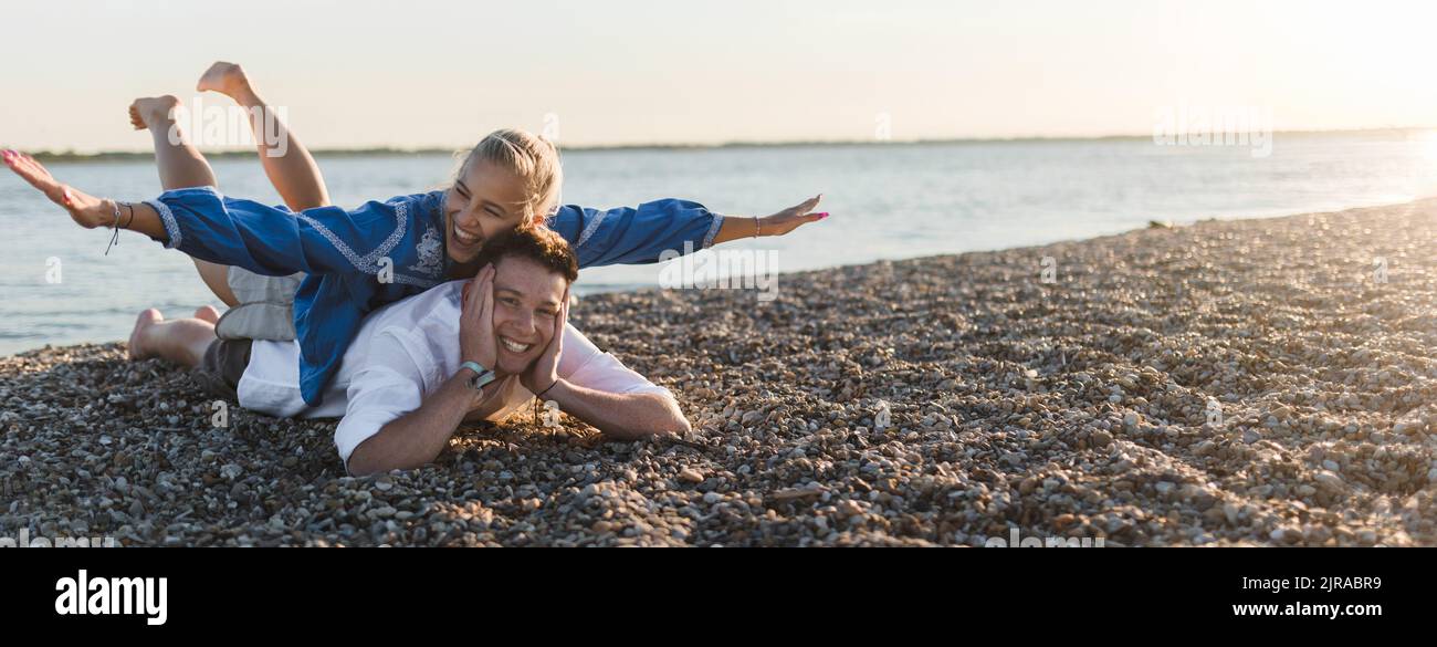 Happy young woman lying on her boyfriends back, looking at camera ...