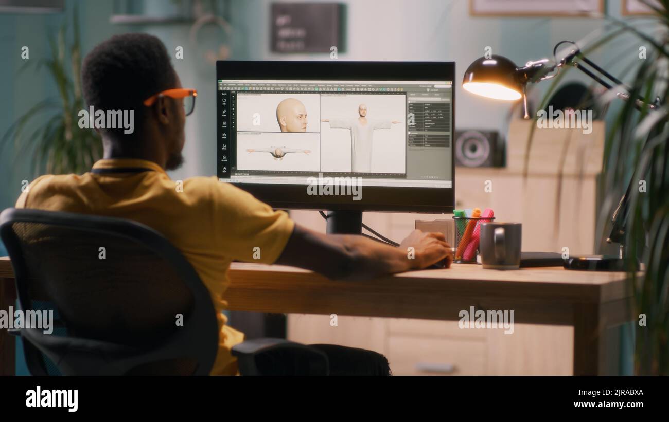 African American man using computer to create 3D model of human for videogame during work from ...