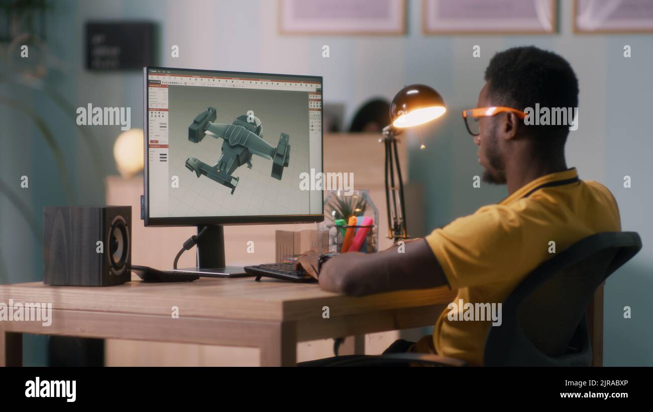 African American man in glasses using computer to create 3D model of aircraft while working at ...