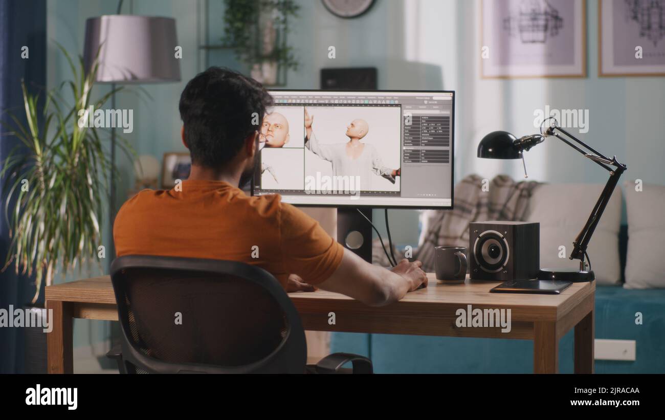 Back view of anonymous man creating 3D model of videogame character while sitting at table and ...