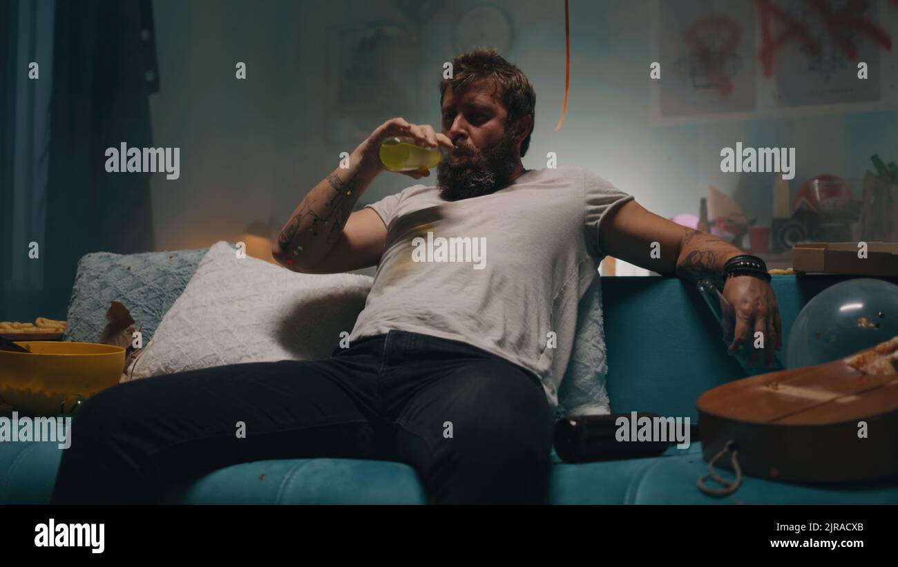 Bearded male drinking alcohol during self isolation while sitting on ...