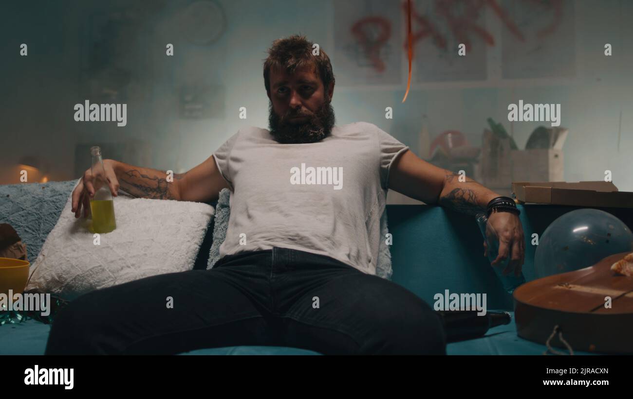 Bearded male drinking alcohol during self isolation while sitting on ...