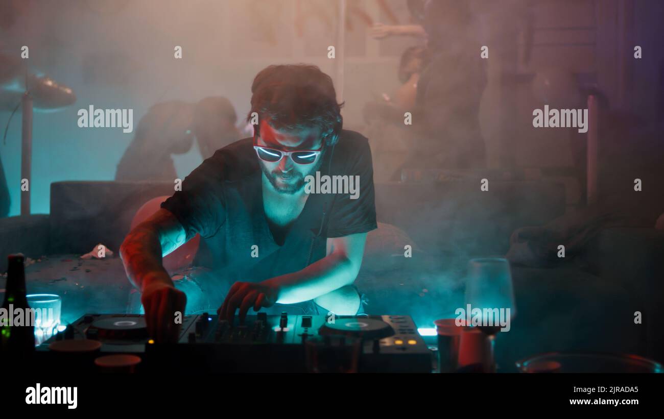Serious male DJ in sunglasses and headphones sitting on sofa near ...
