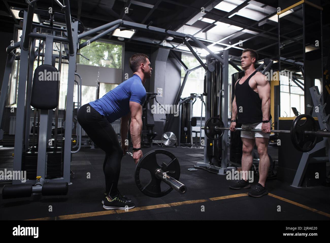 Twin brothers muscular athletes lifting heavy barbells, standing face ...