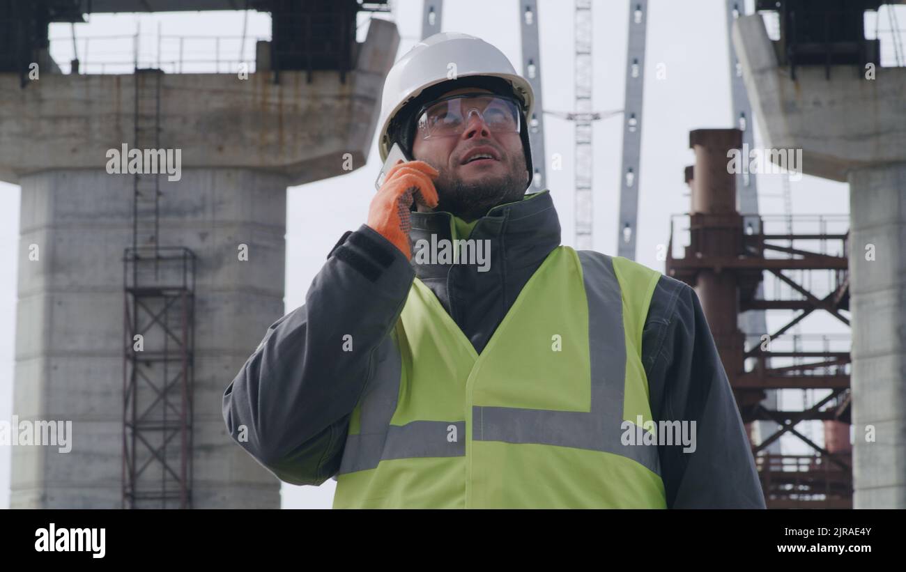 Man in hardhat and goggles inspecting unfinished bridge and talking on ...