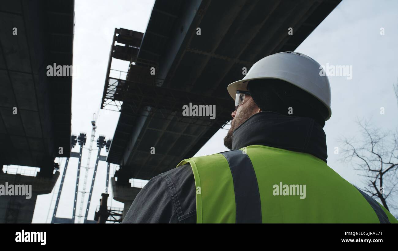Adult man in hardhat examining concrete structure of unfinished bridge ...