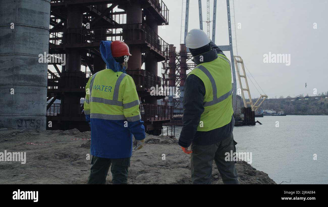Men in uniform inspecting unfinished bridge over river while working on ...