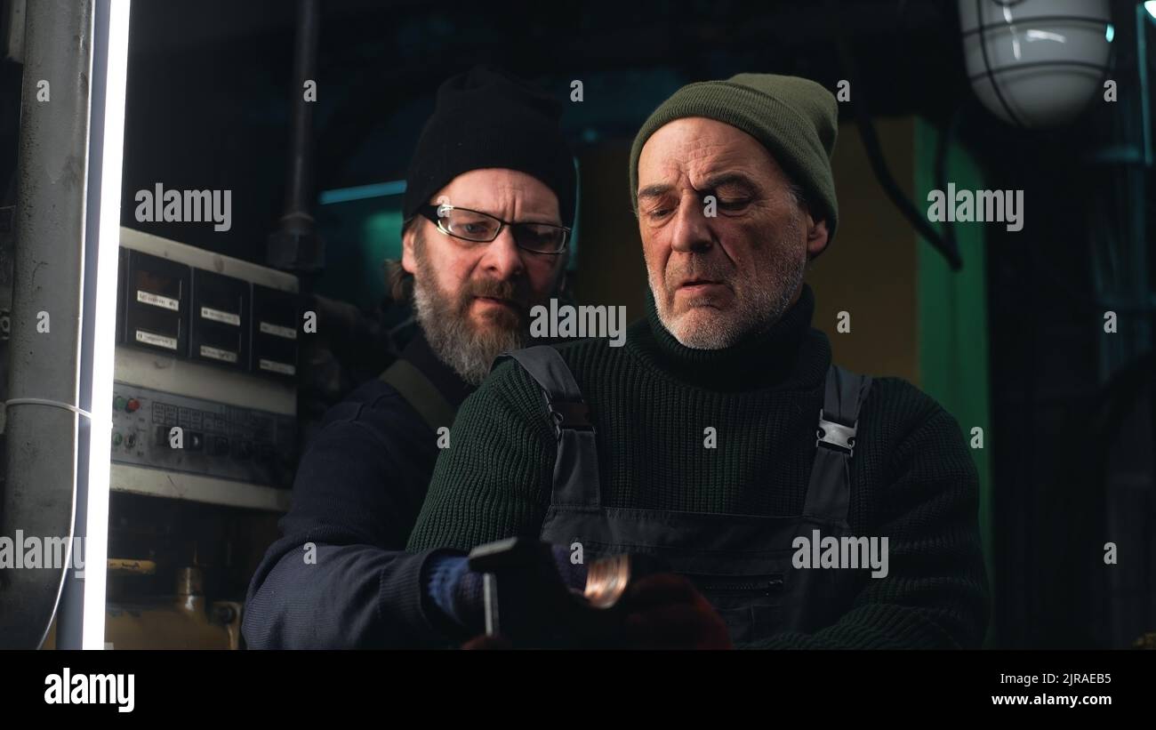 Displeased bearded man helping senior colleague to inspect metal part ...