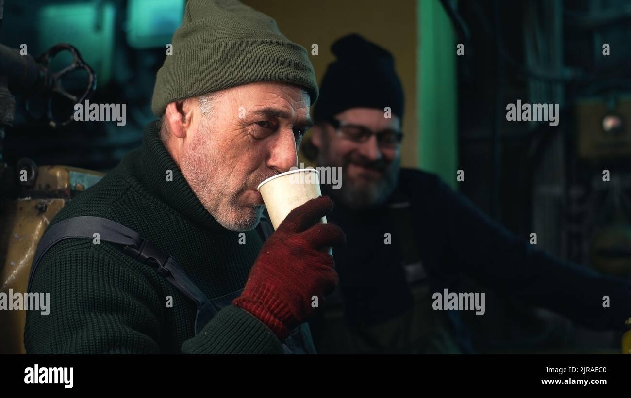 Aged man laughing and drinking then talking and giving cup to coworker ...