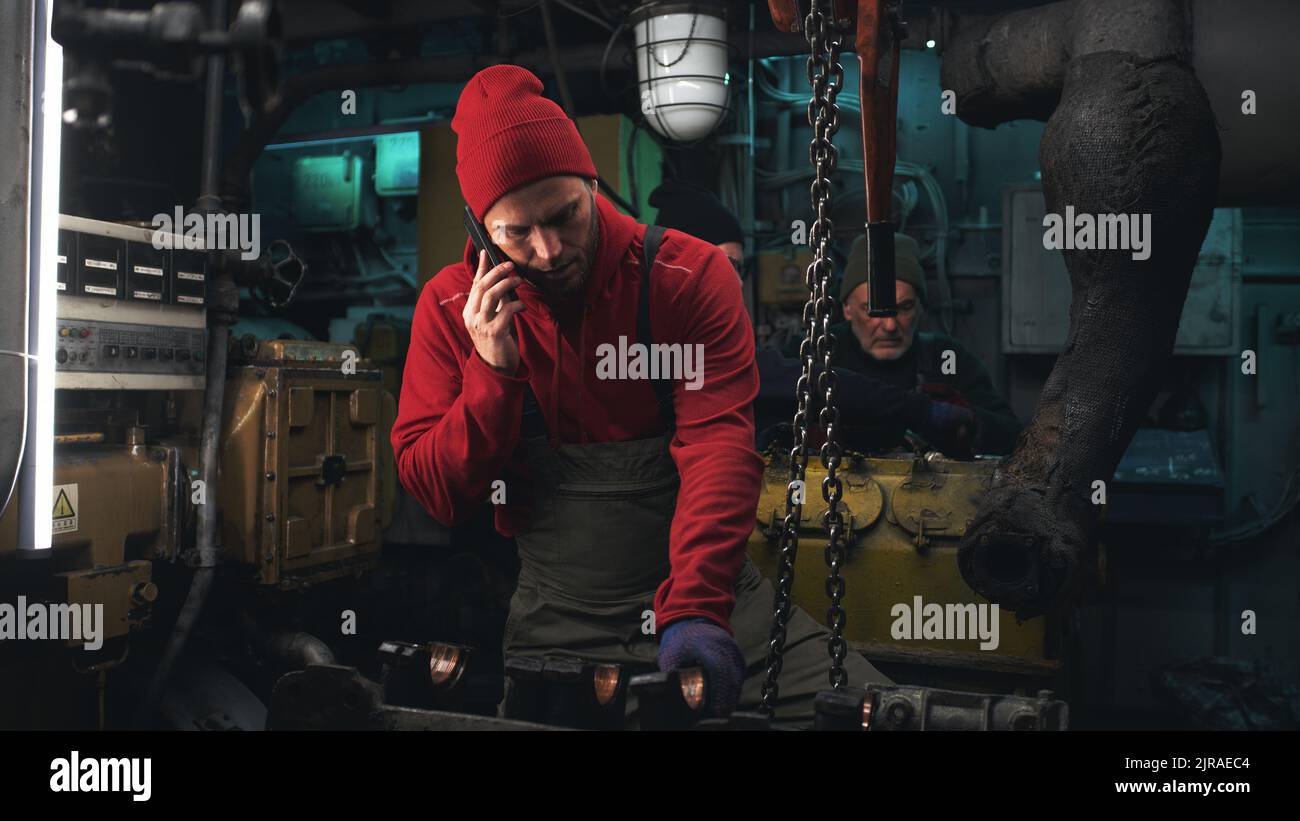 Zoom in view of male engineer making phone call while repairing motor ...