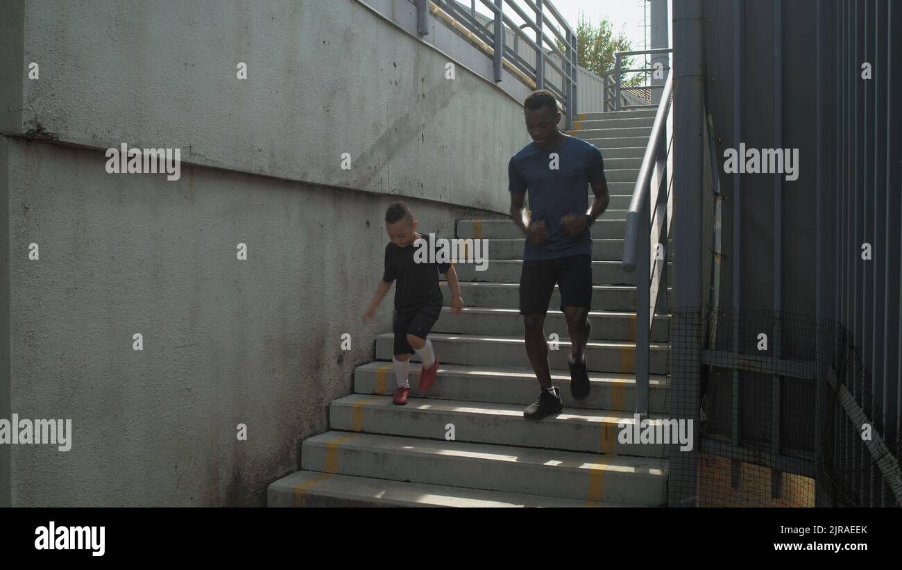 Pan left of black man and mixed race boy running on staircase during ...