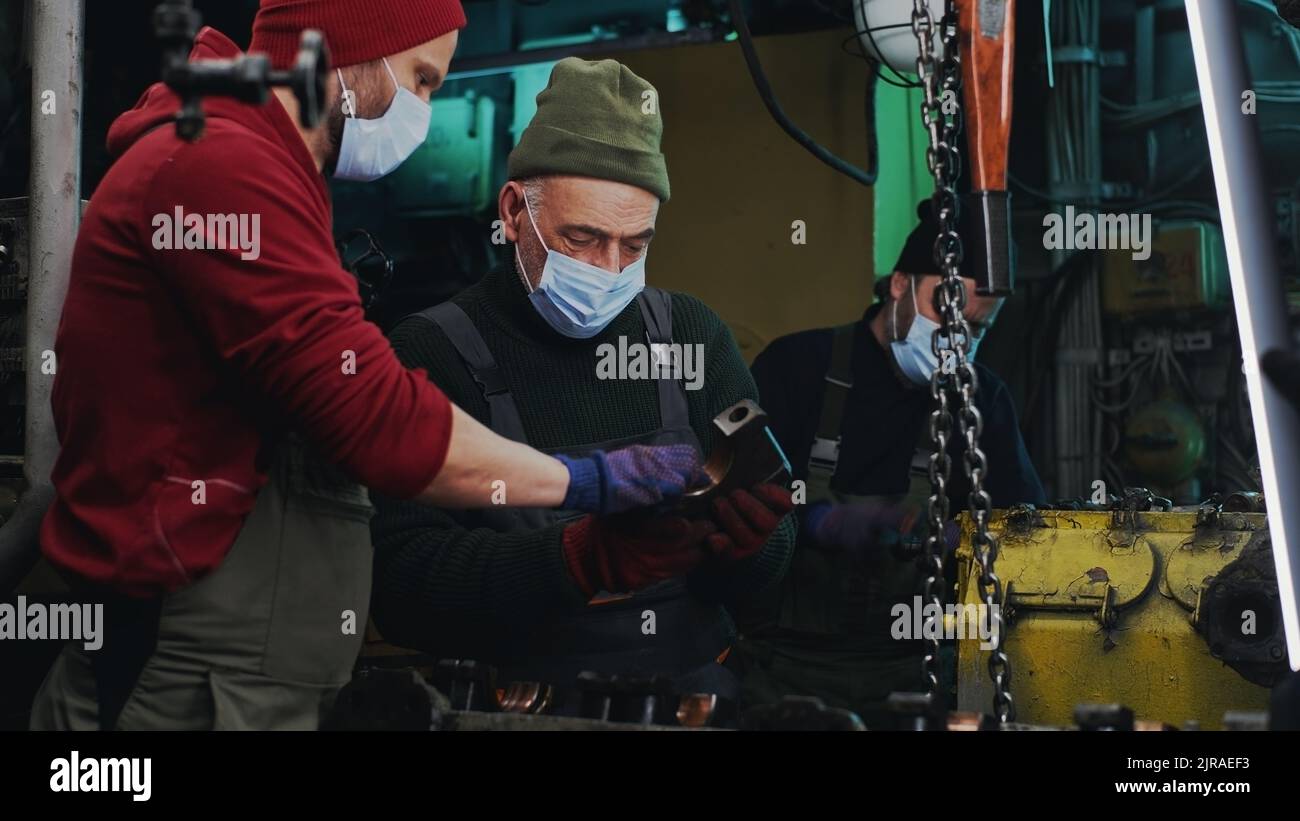 Men in medical masks examining metal part while fixing motor in engine ...
