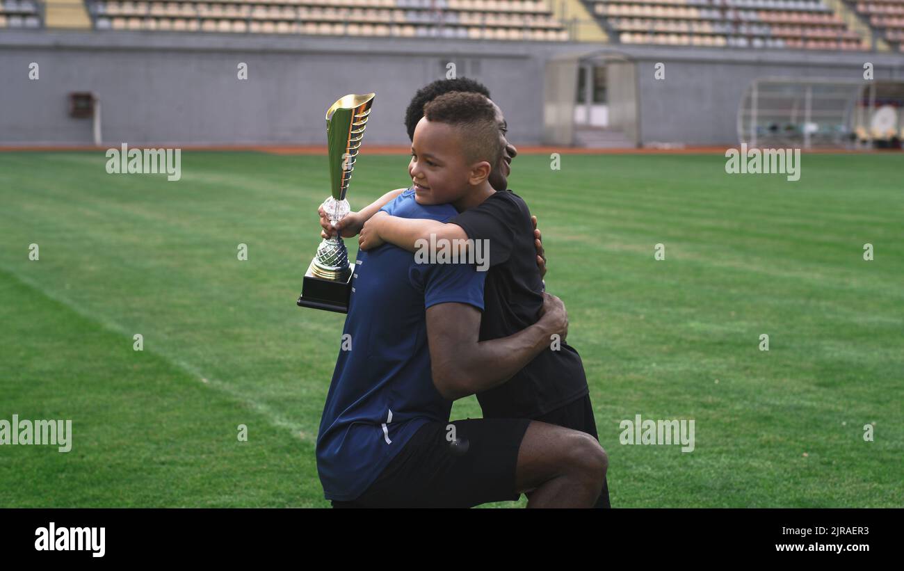 African American man giving trophy and speaking with mixed race boy ...