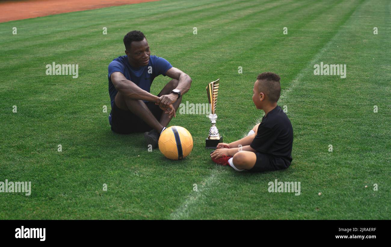 Zoom in view of black man and mixed race boy sitting near trophy and ...
