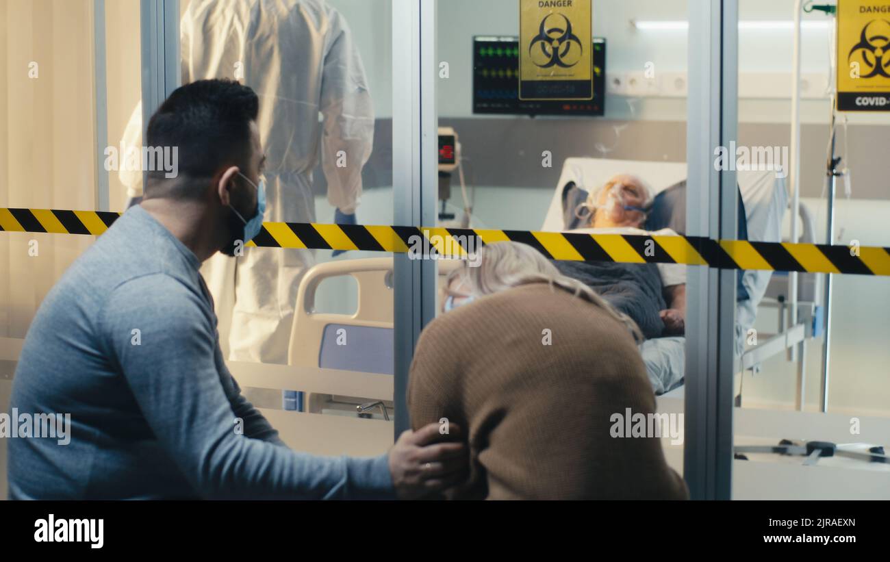 Man in mask supporting crying woman while sitting near glass wall of ...