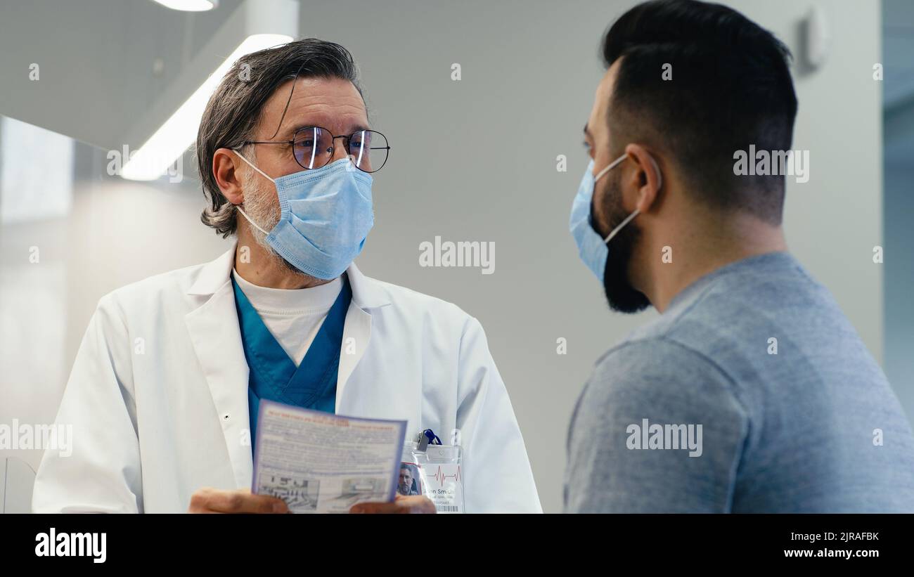 Middle aged male medical practitioner in mask talking and giving ...