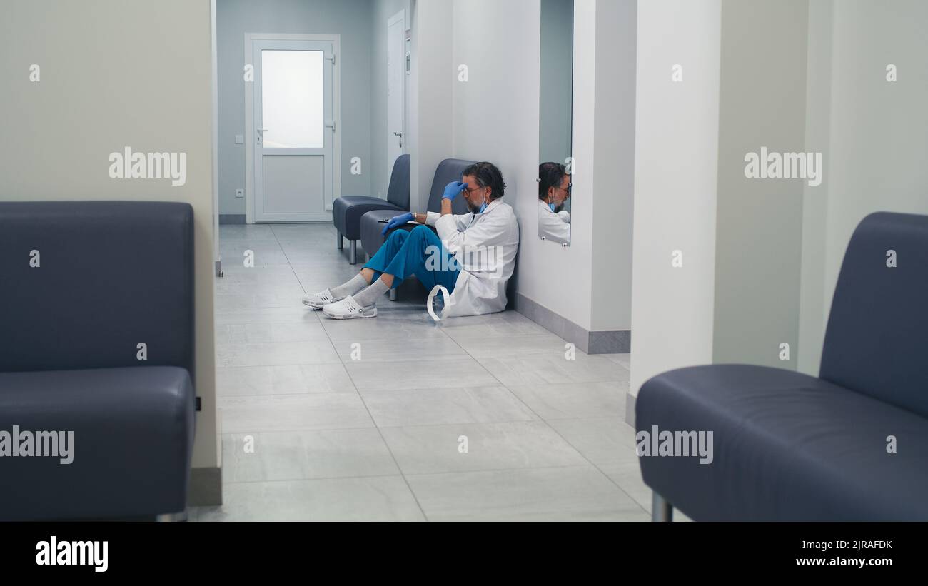 Tired middle aged medical practitioner taking off face shield and ...