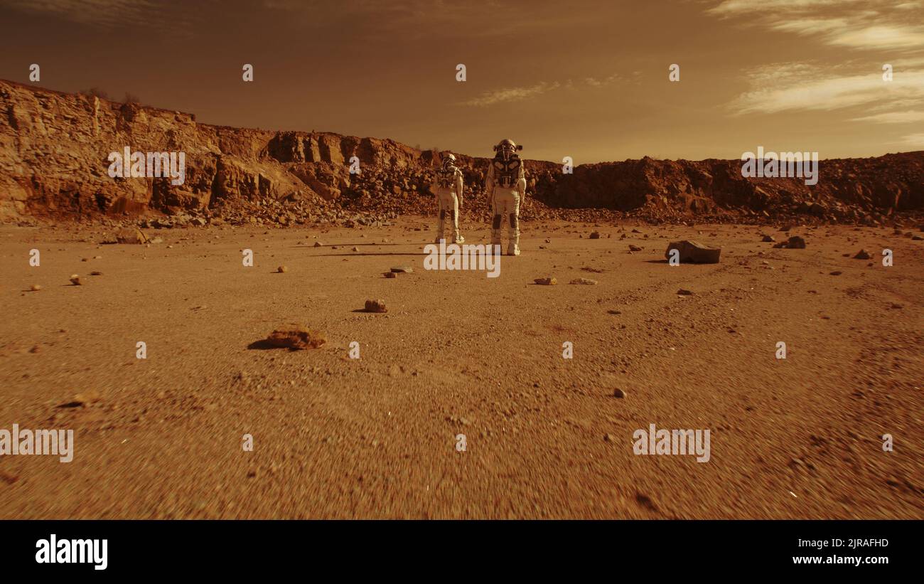 Tracking shot of anonymous people in spacesuits walking on arid ground ...