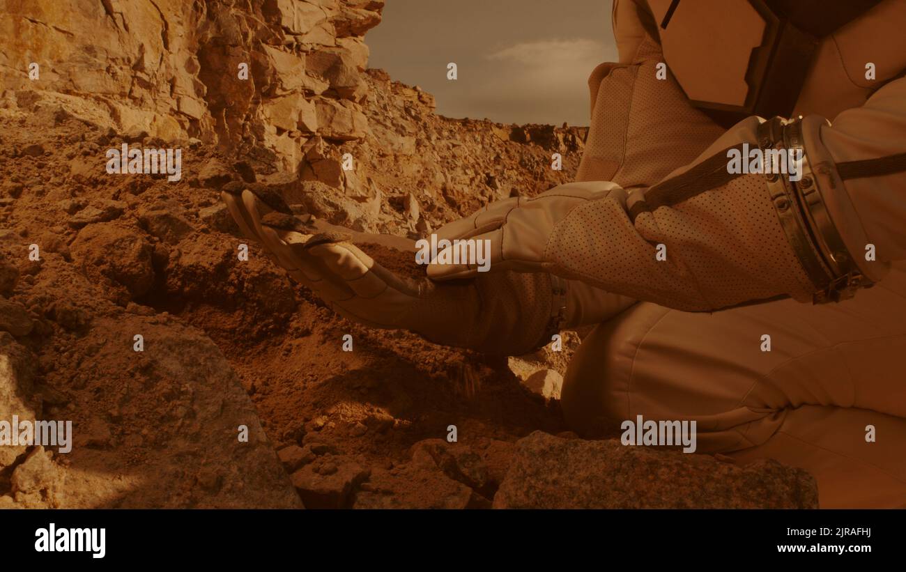 Crop astronaut in protective spacesuit digging and inspecting soil ...