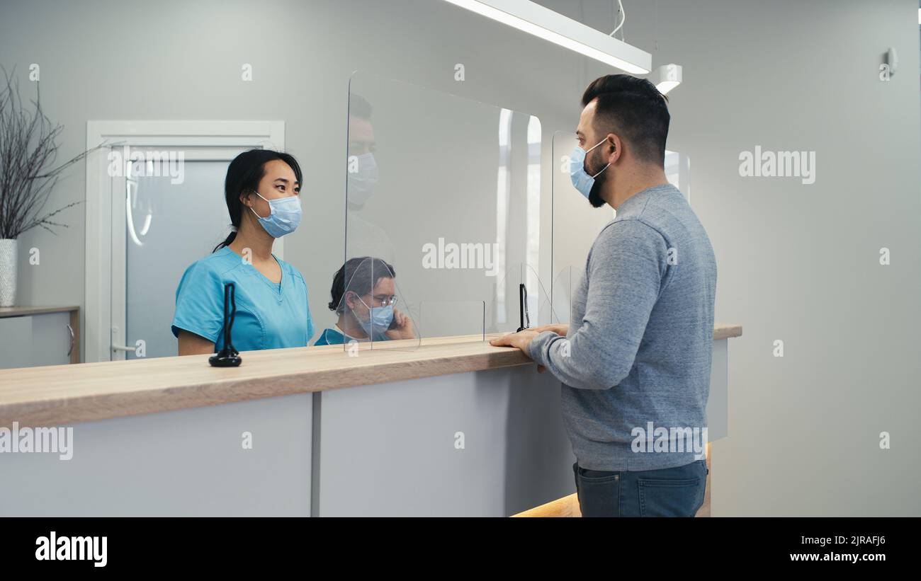 Male patient in mask asking question to female receptionist then ...