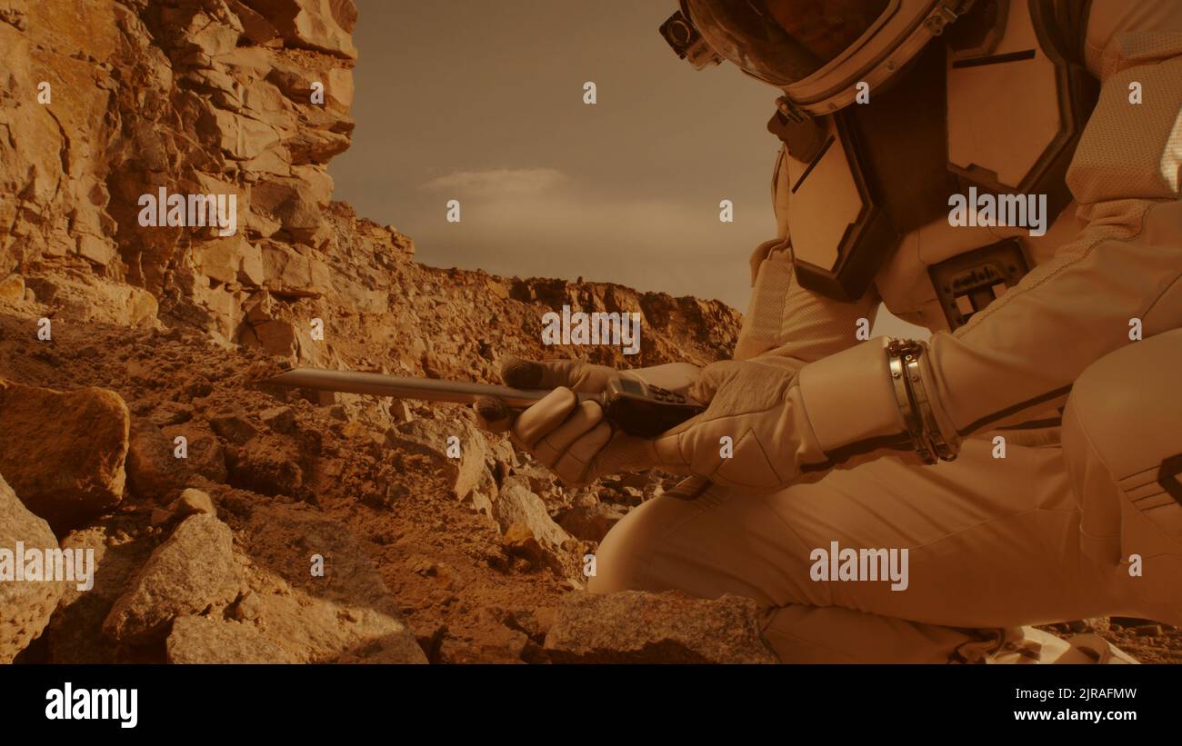 Crop cosmonaut in suit taking sample of soil with analyzer near ...