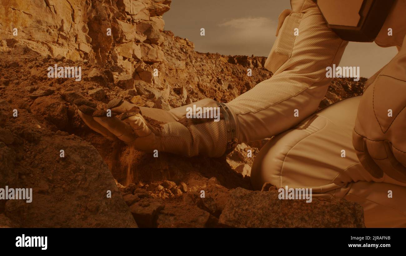 Crop astronaut in protective spacesuit digging and inspecting soil ...